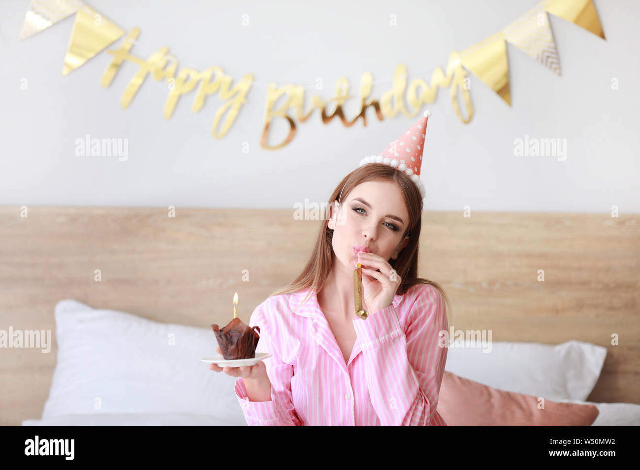 Happy woman with Birthday cake and party whistle in bedroom at home ...