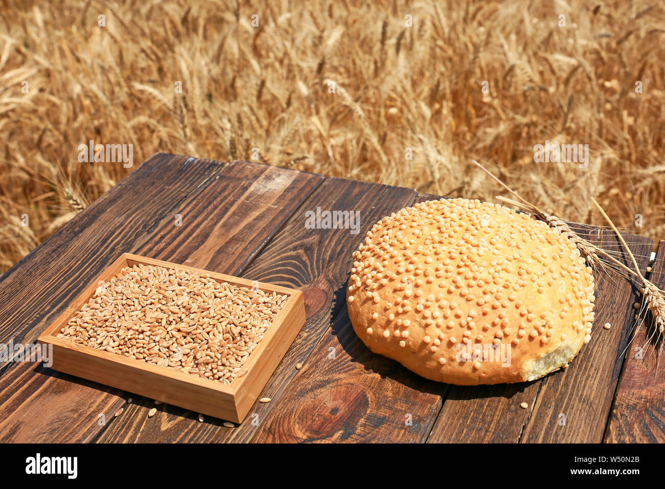Wheat grains with bread on wooden table in field Stock Photo - Alamy
