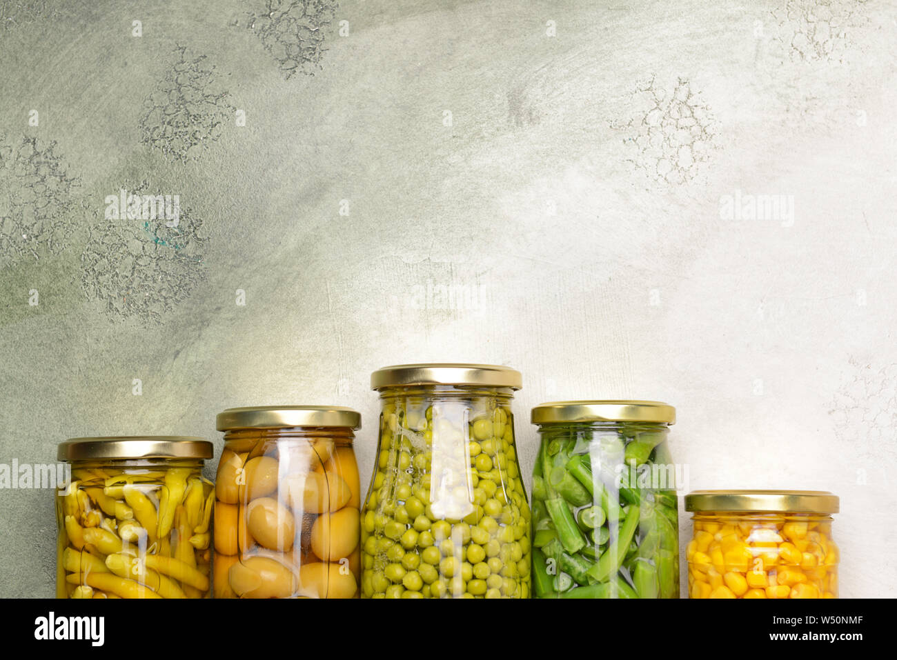 Jars with different canned vegetables and legumes on light background ...