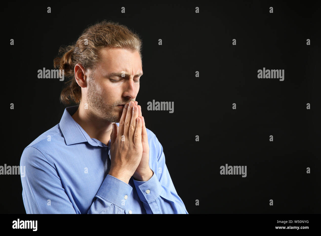 Religious young man praying on dark background Stock Photo - Alamy