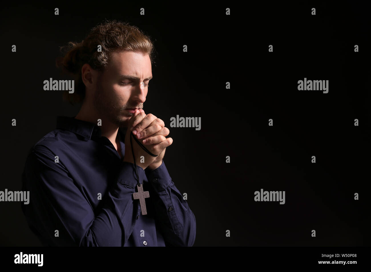 Religious young man praying on dark background Stock Photo - Alamy