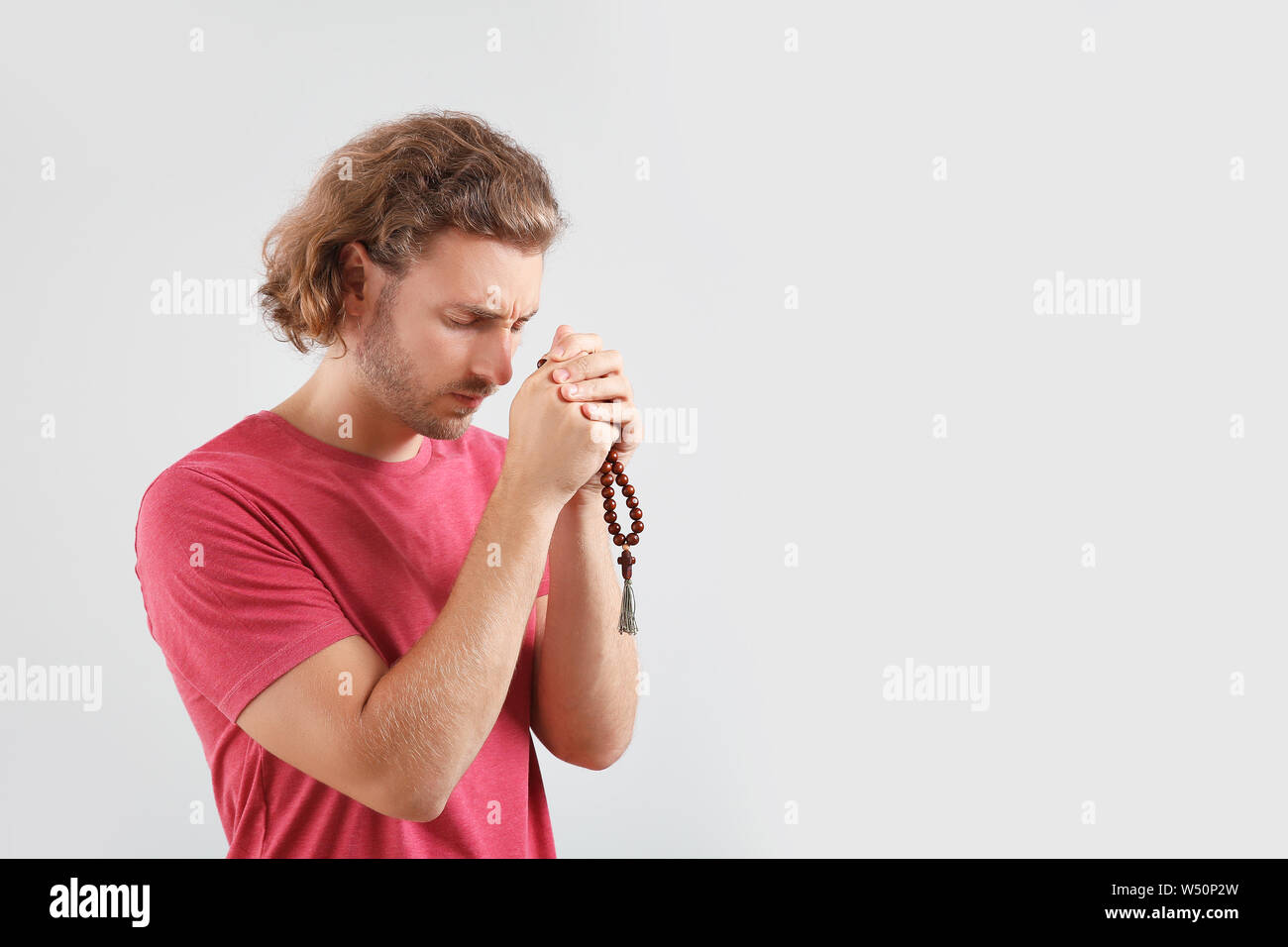 Religious young man praying on light background Stock Photo - Alamy