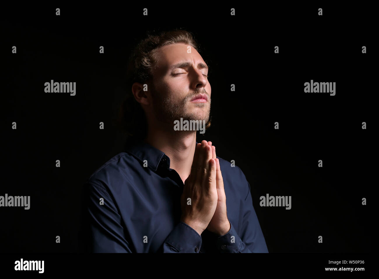 Religious young man praying on dark background Stock Photo - Alamy
