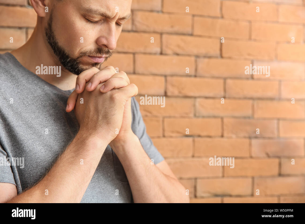 Religious man praying against brick wall Stock Photo - Alamy