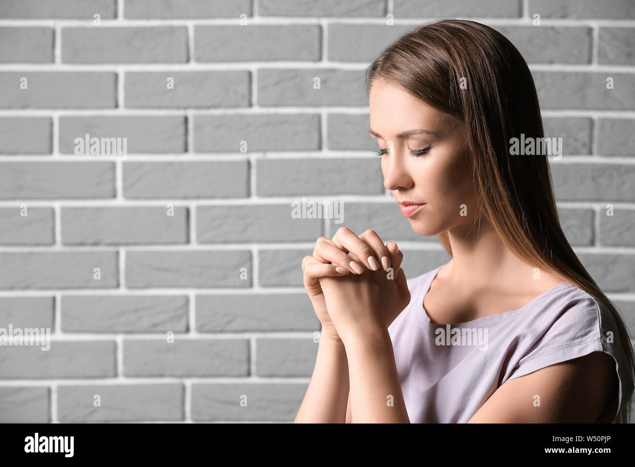 Religious young woman praying against brick wall Stock Photo - Alamy