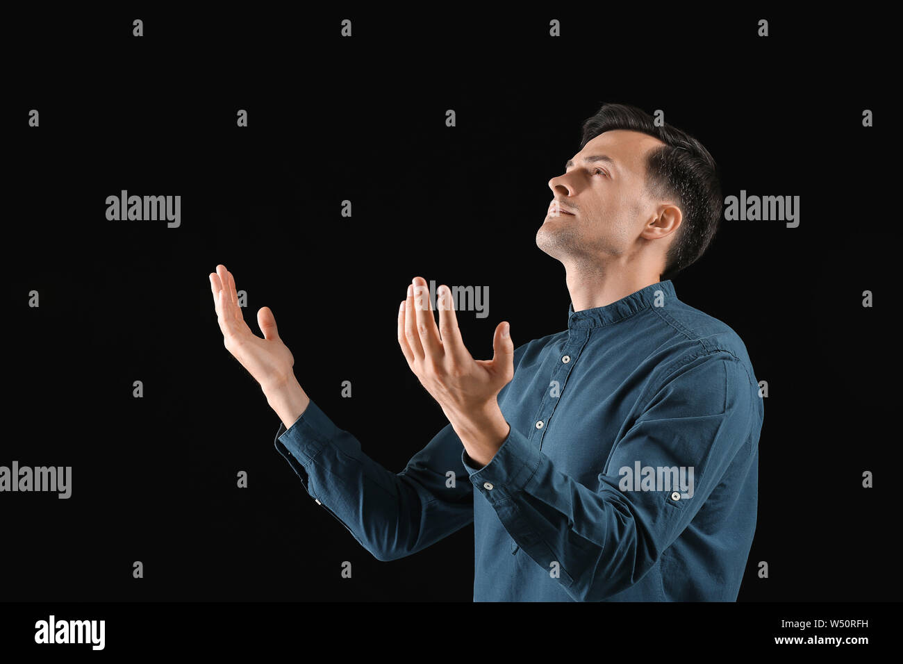 Religious man praying to God on dark background Stock Photo - Alamy