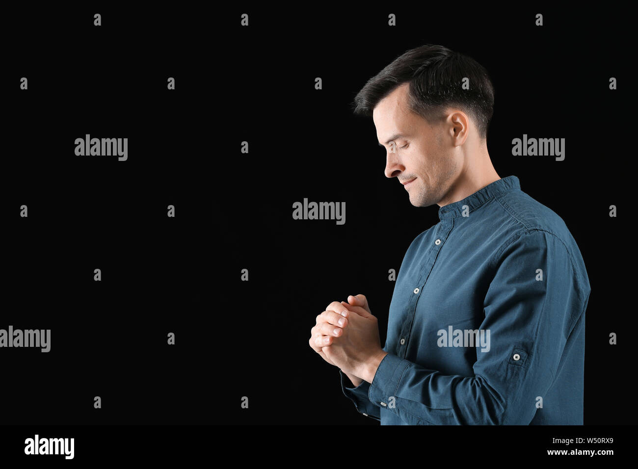 Religious man praying to God on dark background Stock Photo - Alamy