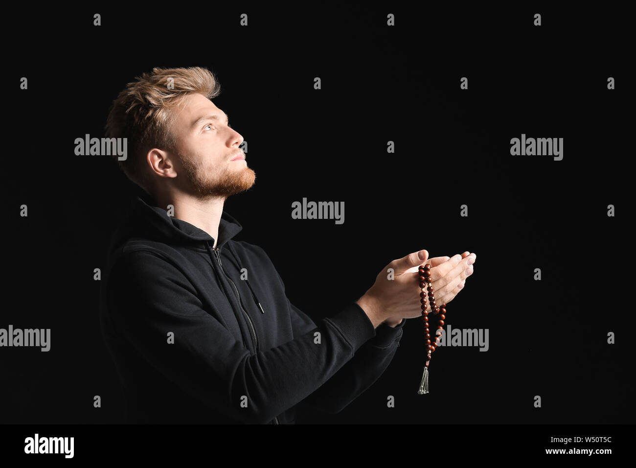 Religious young man praying to God on dark background Stock Photo - Alamy