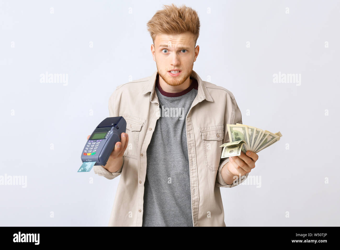 Confused young man with credit card payment terminal and dollars on ...