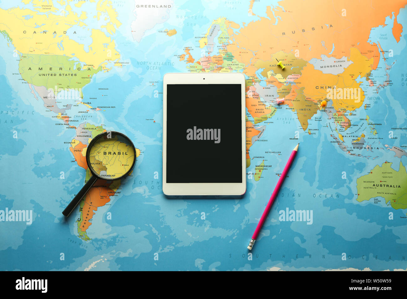 Tablet computer, pencil and magnifier on world map Stock Photo - Alamy