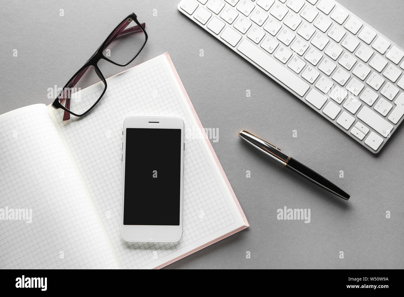 Notebook, mobile phone, glasses, pen and PC keyboard on grey background ...
