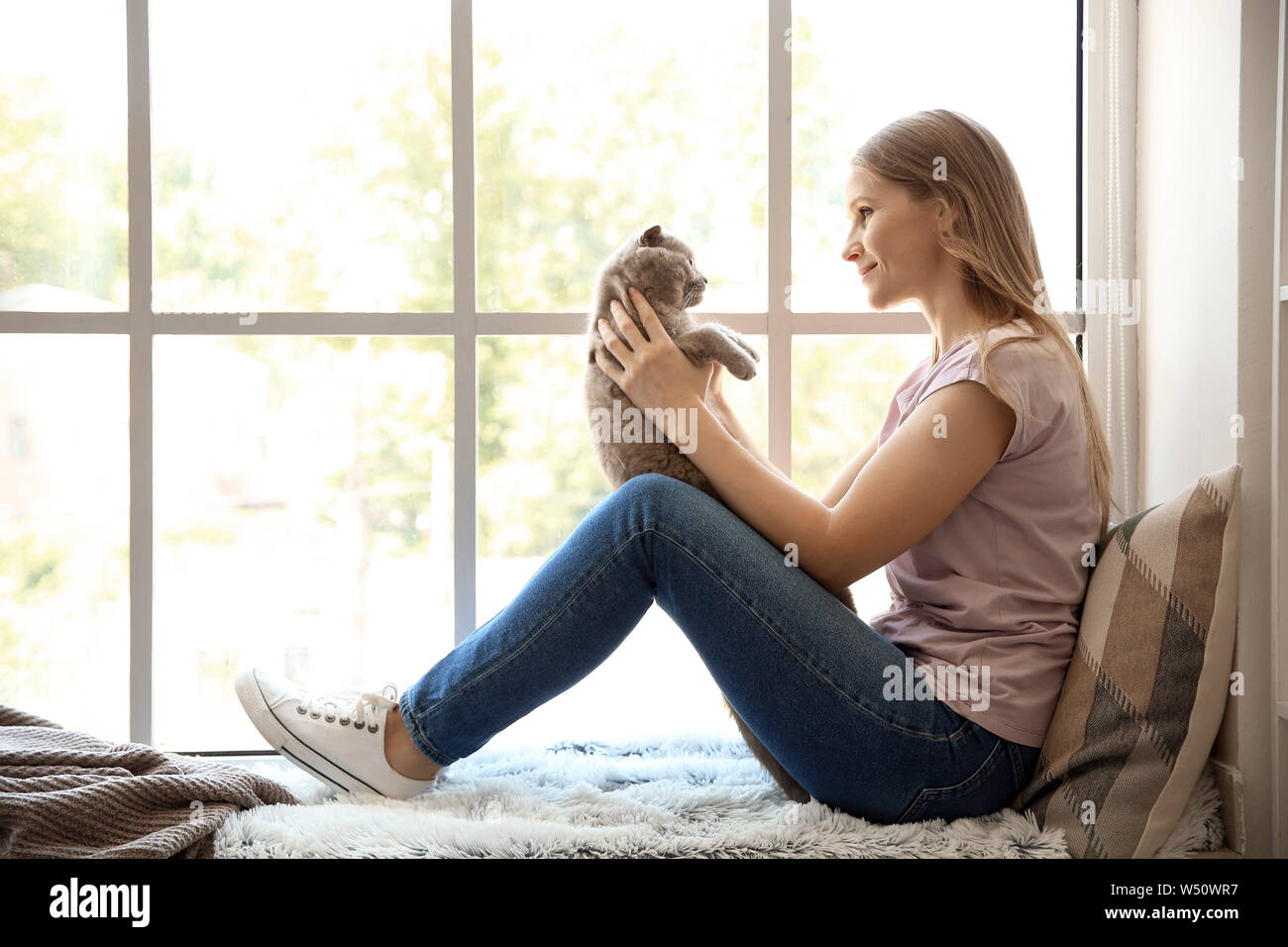 Beautiful woman with cute cat sitting near window Stock Photo - Alamy