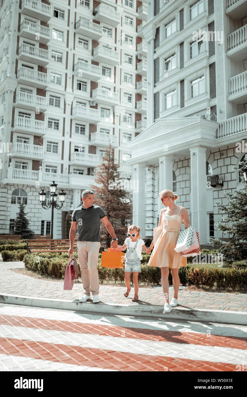 Going home. Small happy family holding hands going to cross the road ...