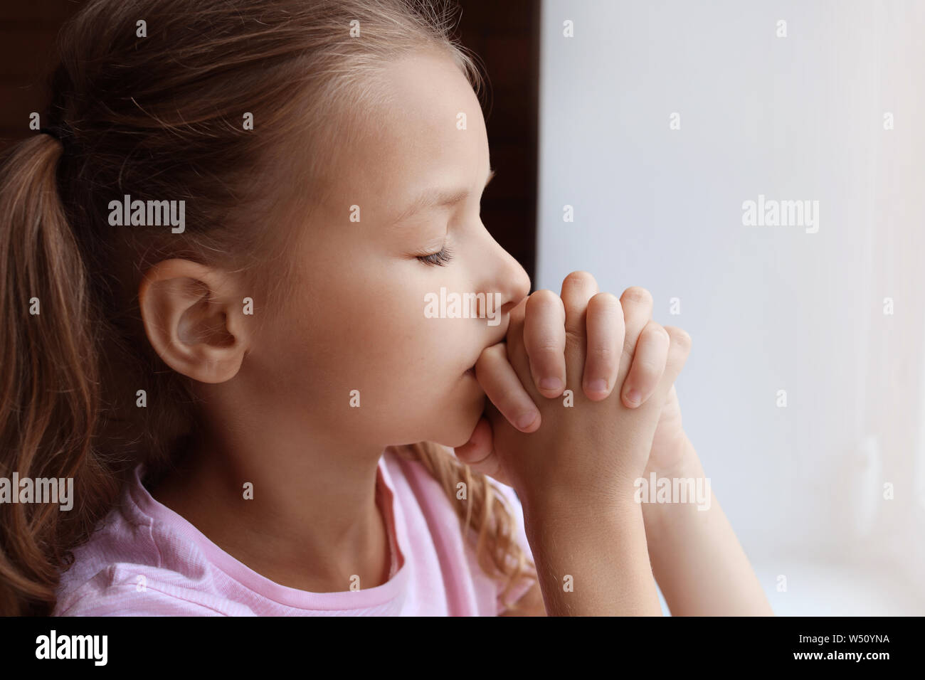 Praying little girl near window Stock Photo - Alamy