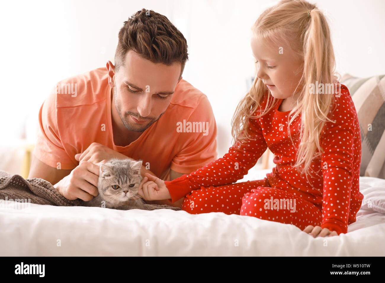 Happy father and daughter with cute cat on bed at home Stock Photo - Alamy