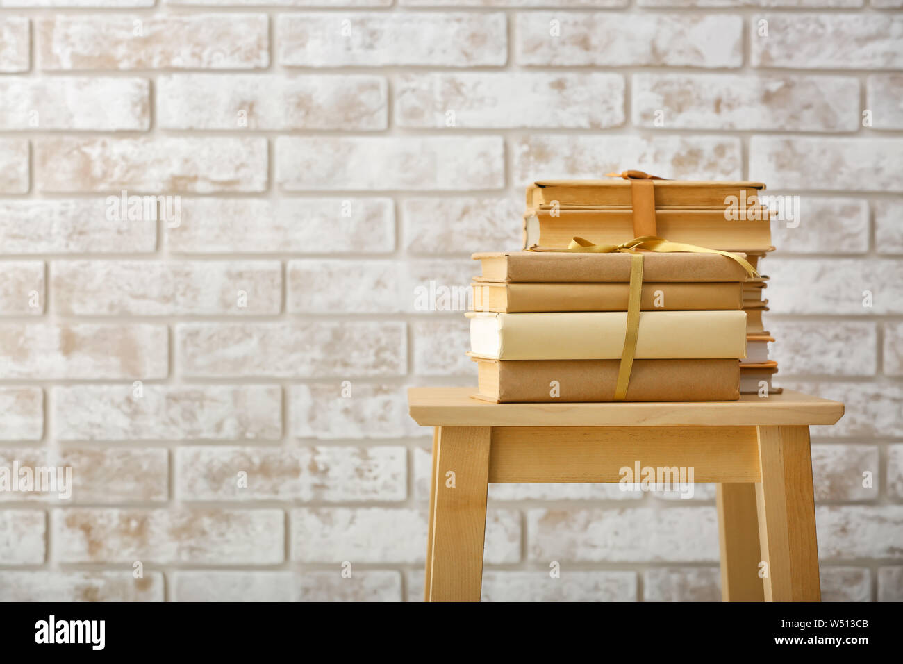 Stacked books on stool against brick wall Stock Photo - Alamy