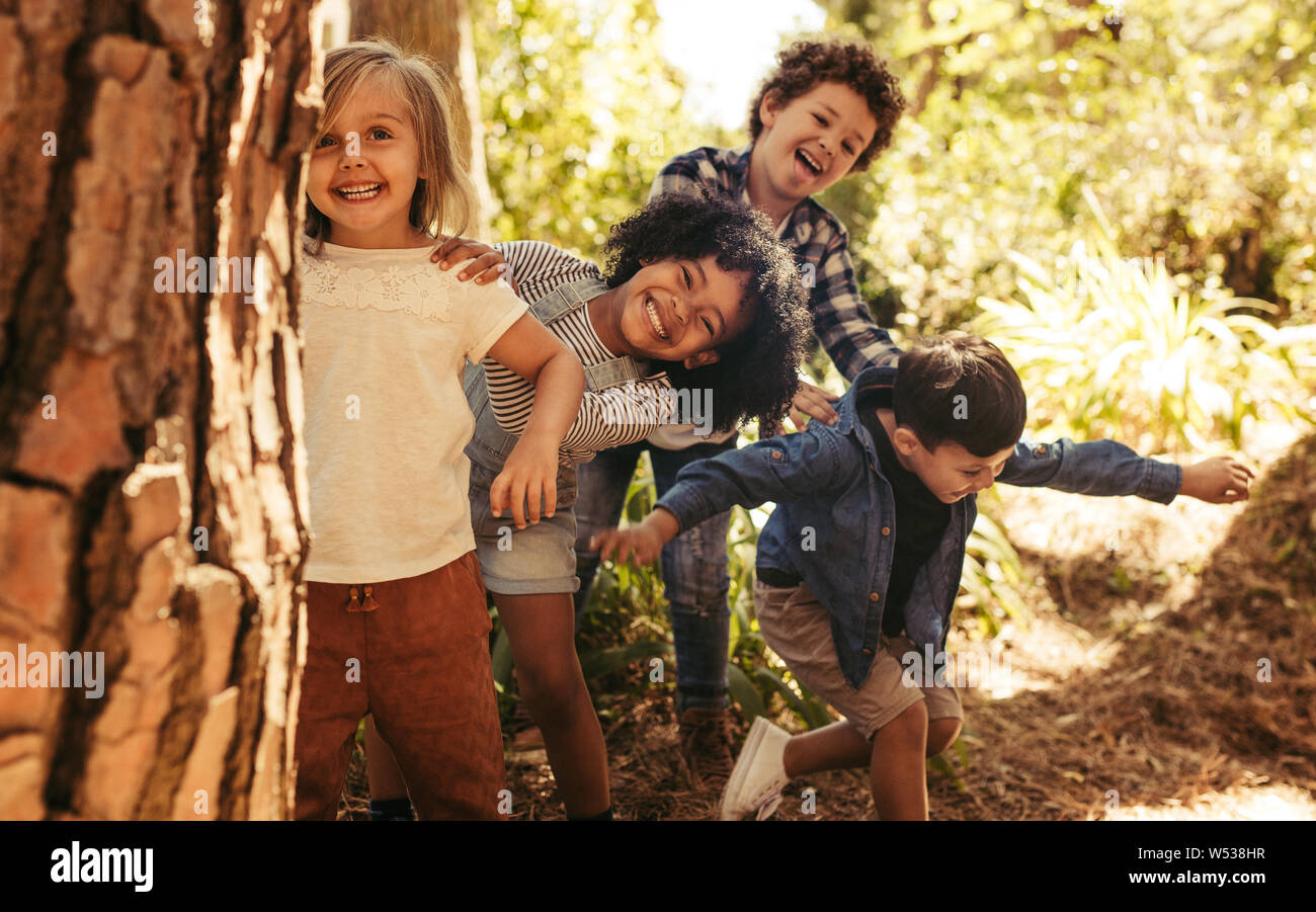 Cute smiling kids peeking out from behind the tree in the park. Group ...