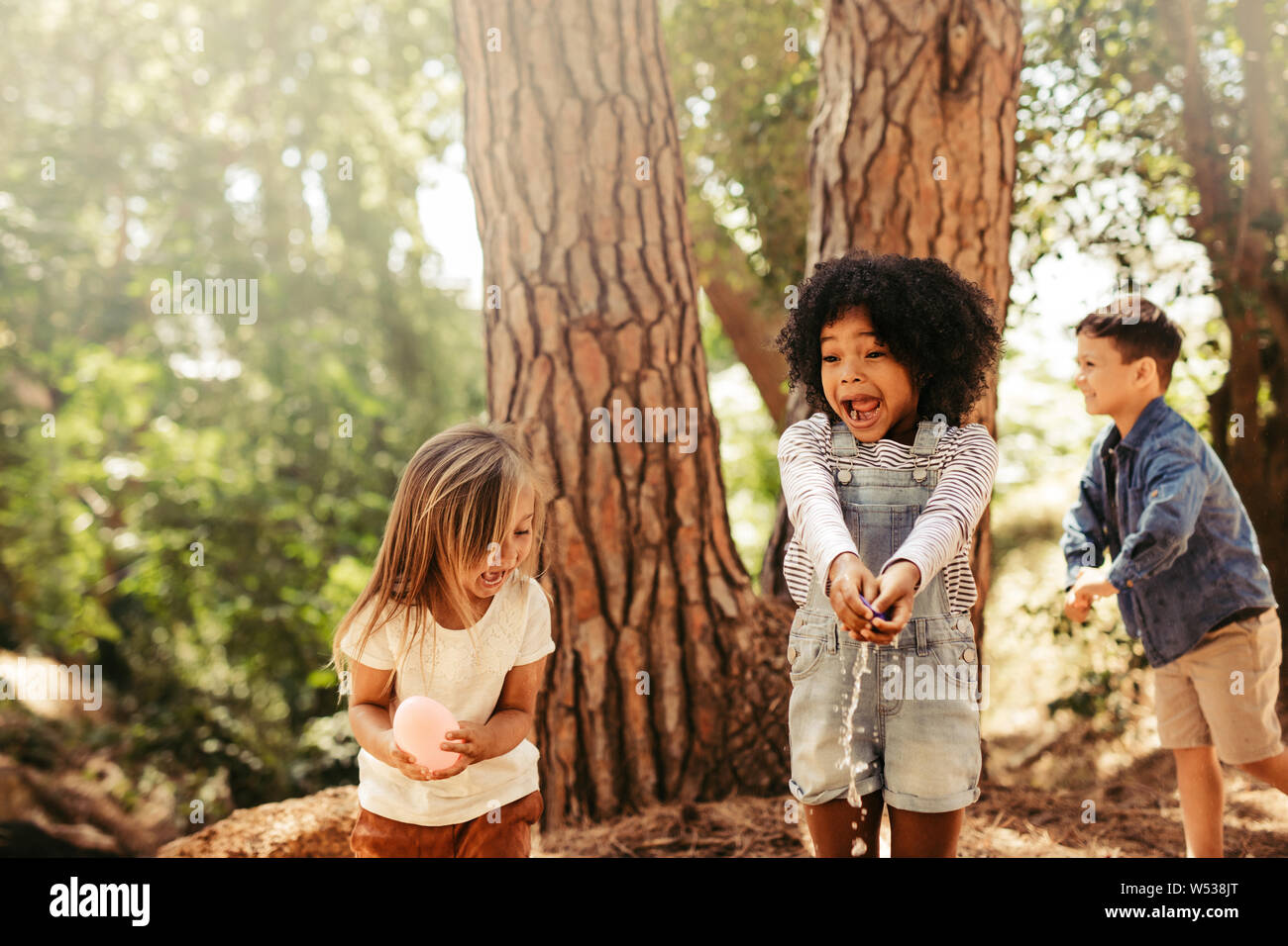 Girls bursting water balloons with hands in a park. Group of kids ...