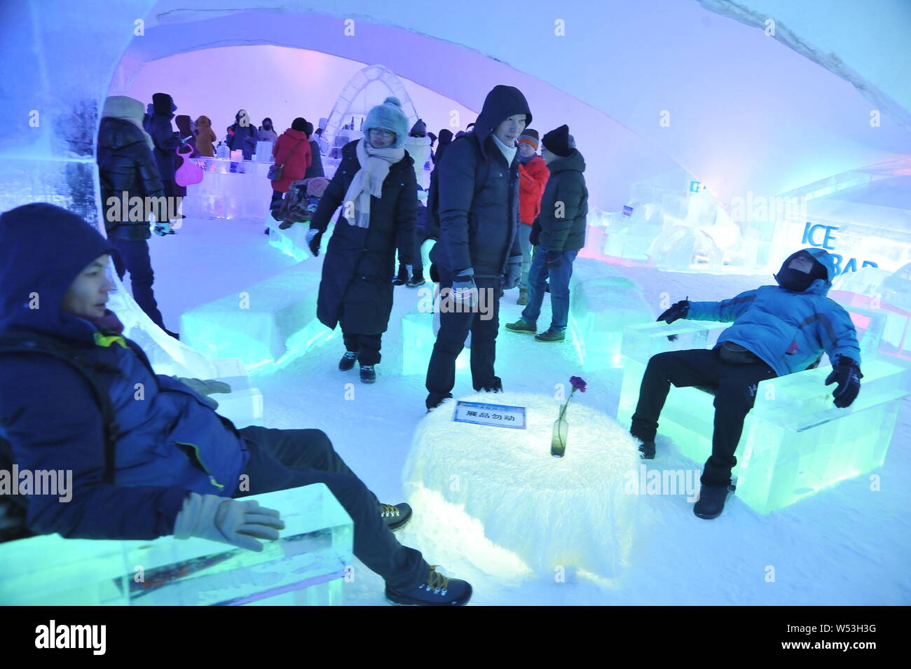 Tourists sit on ice chairs at an arch-shaped ice bar built with ...