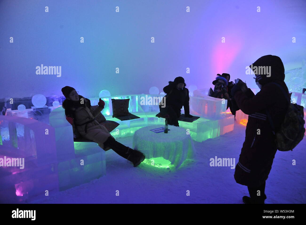 Tourists sit on ice chairs at an arch-shaped ice bar built with ...