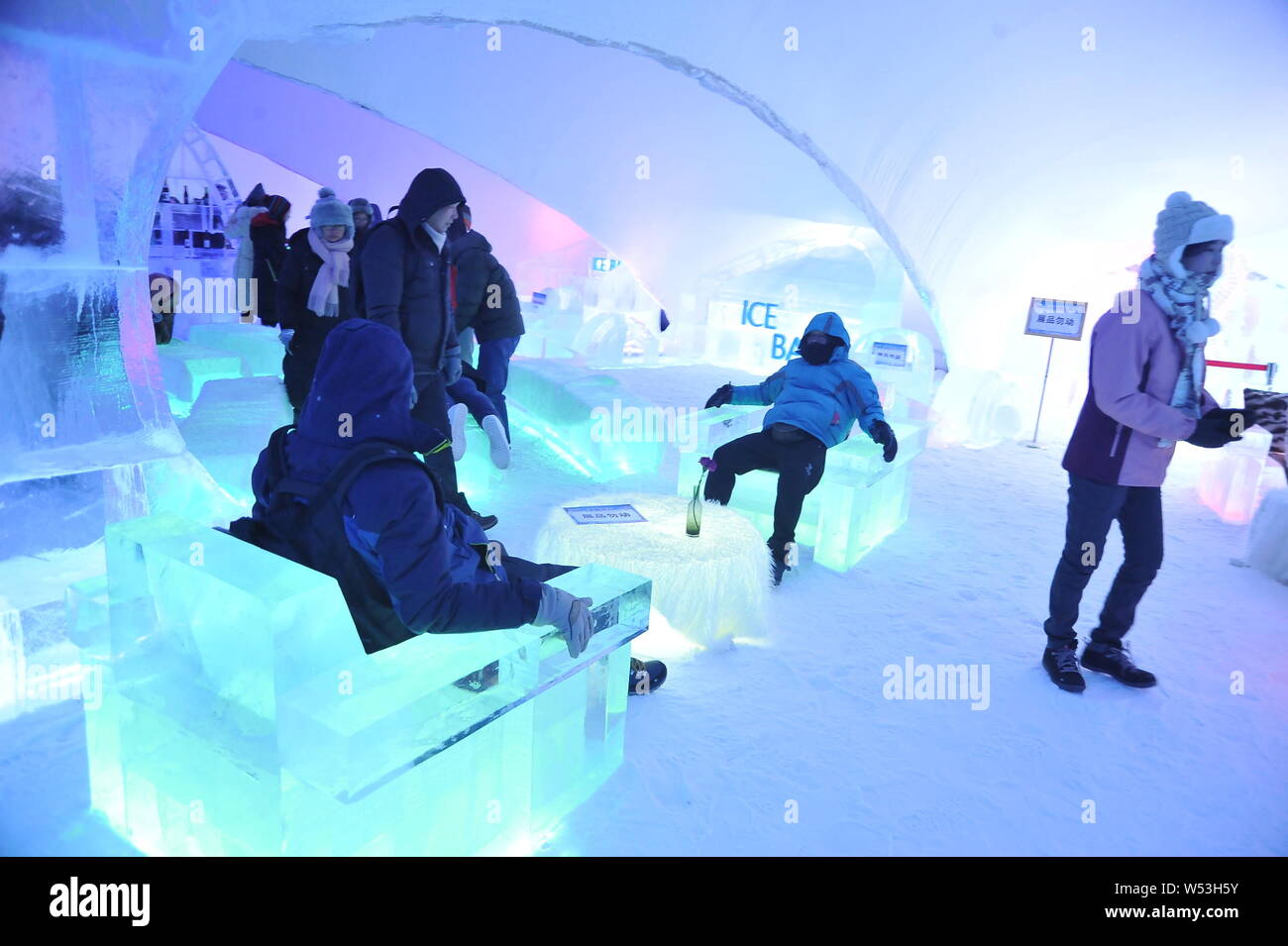 Tourists sit on ice chairs at an arch-shaped ice bar built with ...