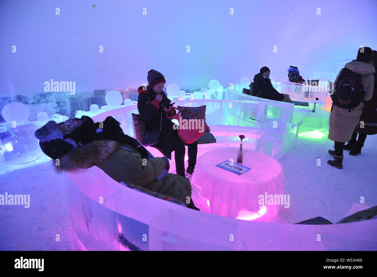 Tourists sit on ice chairs at an arch-shaped ice bar built with ...