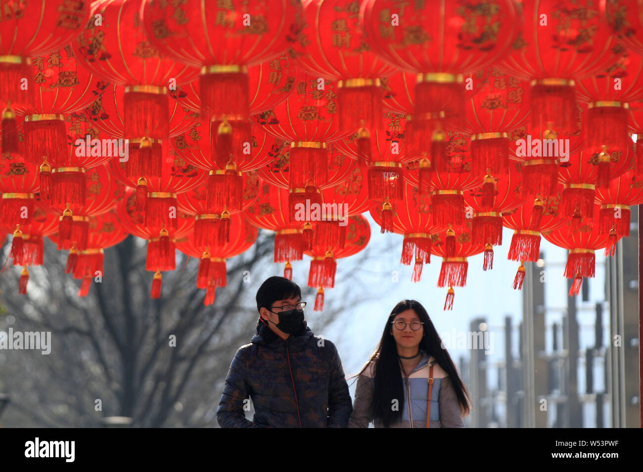 A Chinese couple walks under rows of red lanterns hung up over a street ...