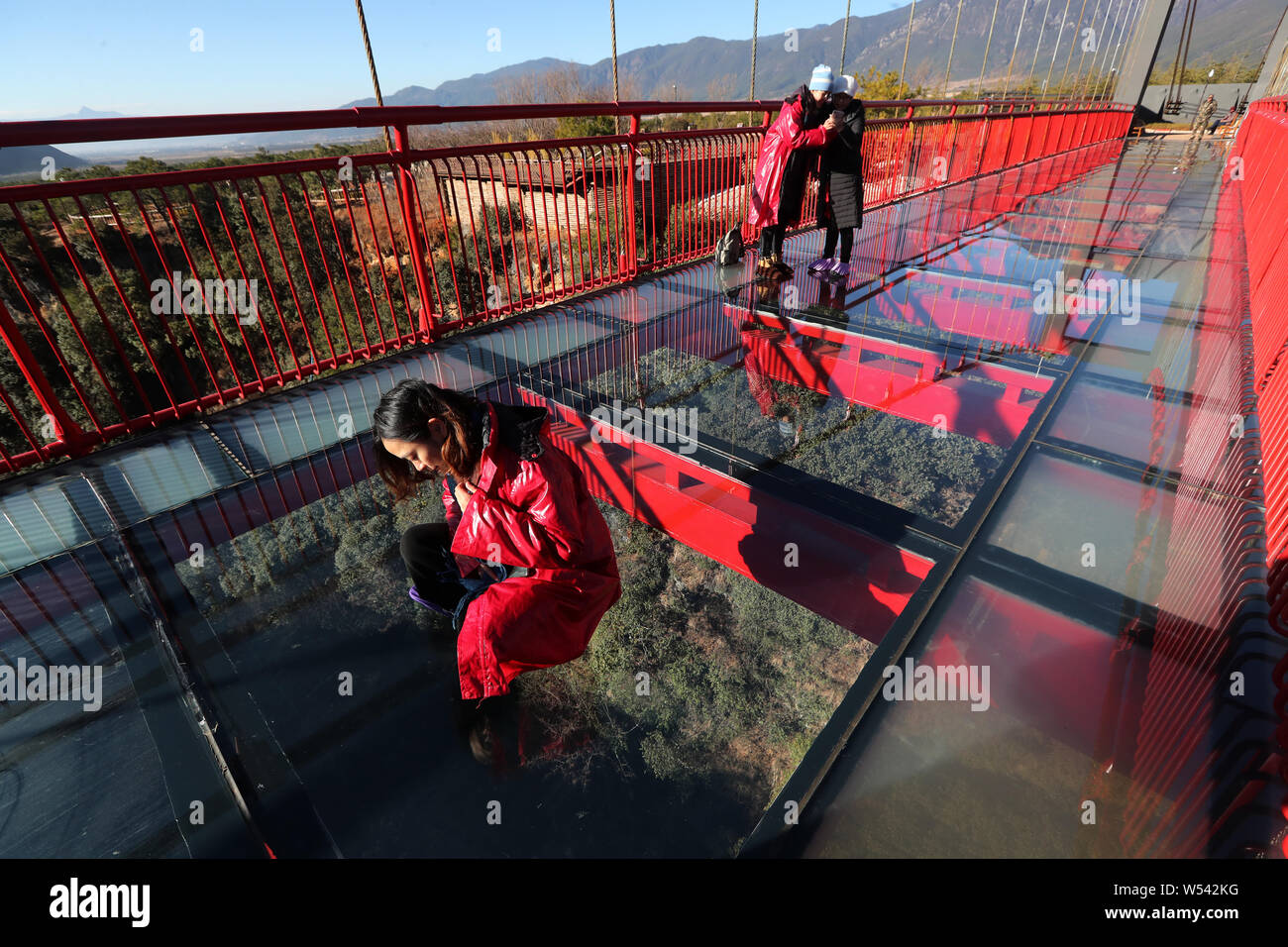 Visitors pose for photos on a glass-bottomed suspension bridge spanning ...