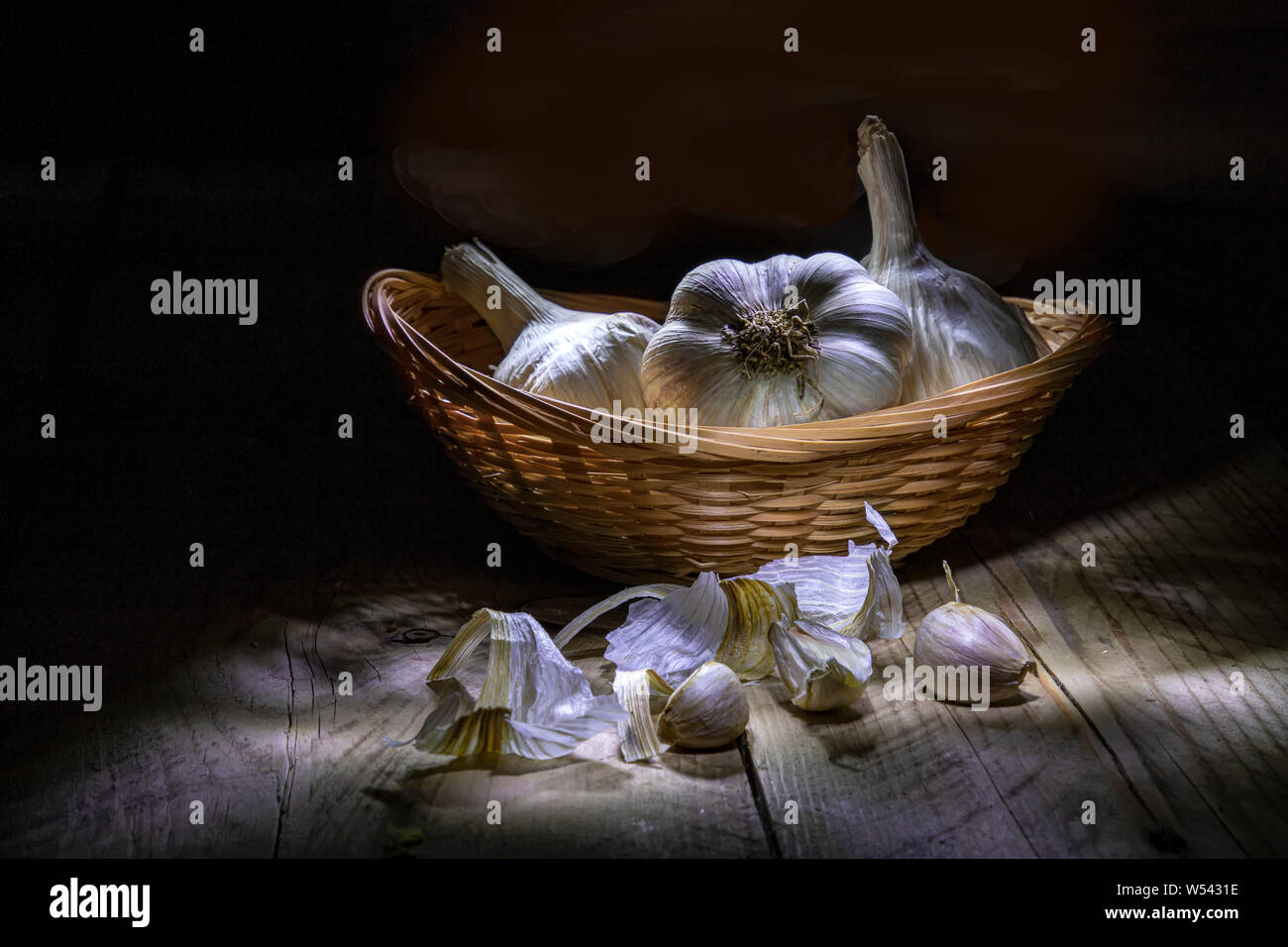Still life on a black background. Garlic in a wicker wooden basket and ...