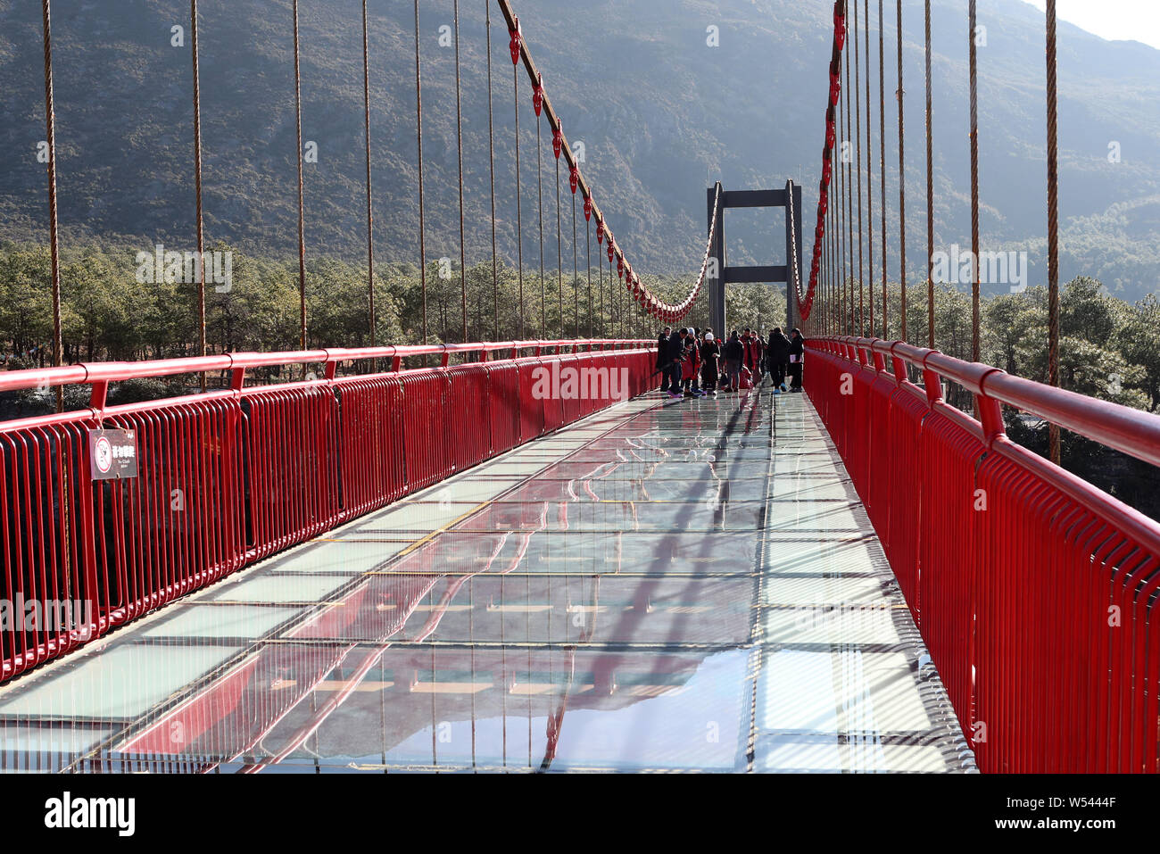 Visitors pose for photos on a glass-bottomed suspension bridge spanning ...