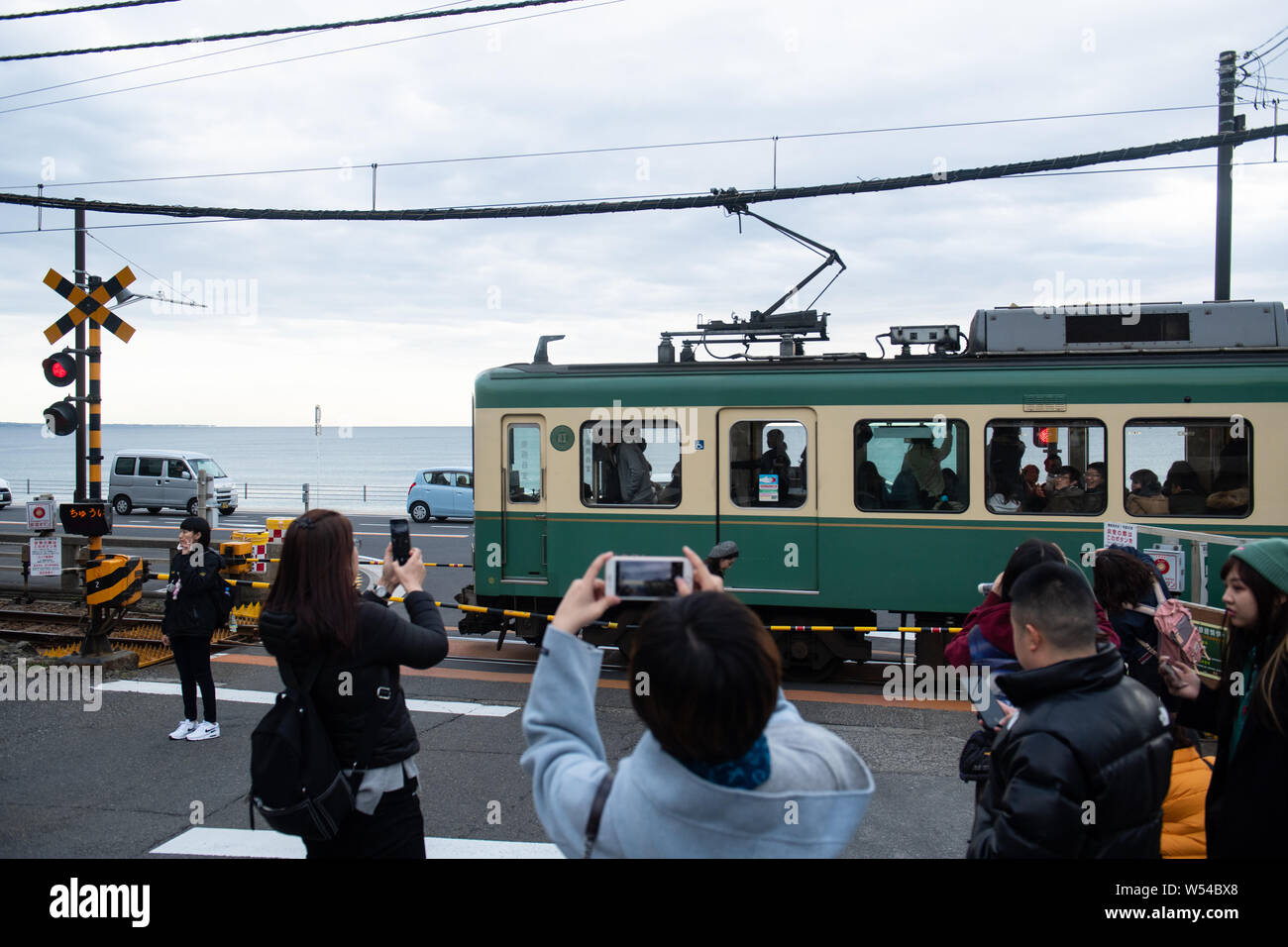 Tourists take photos as a train on the Enoden Line travels past the ...