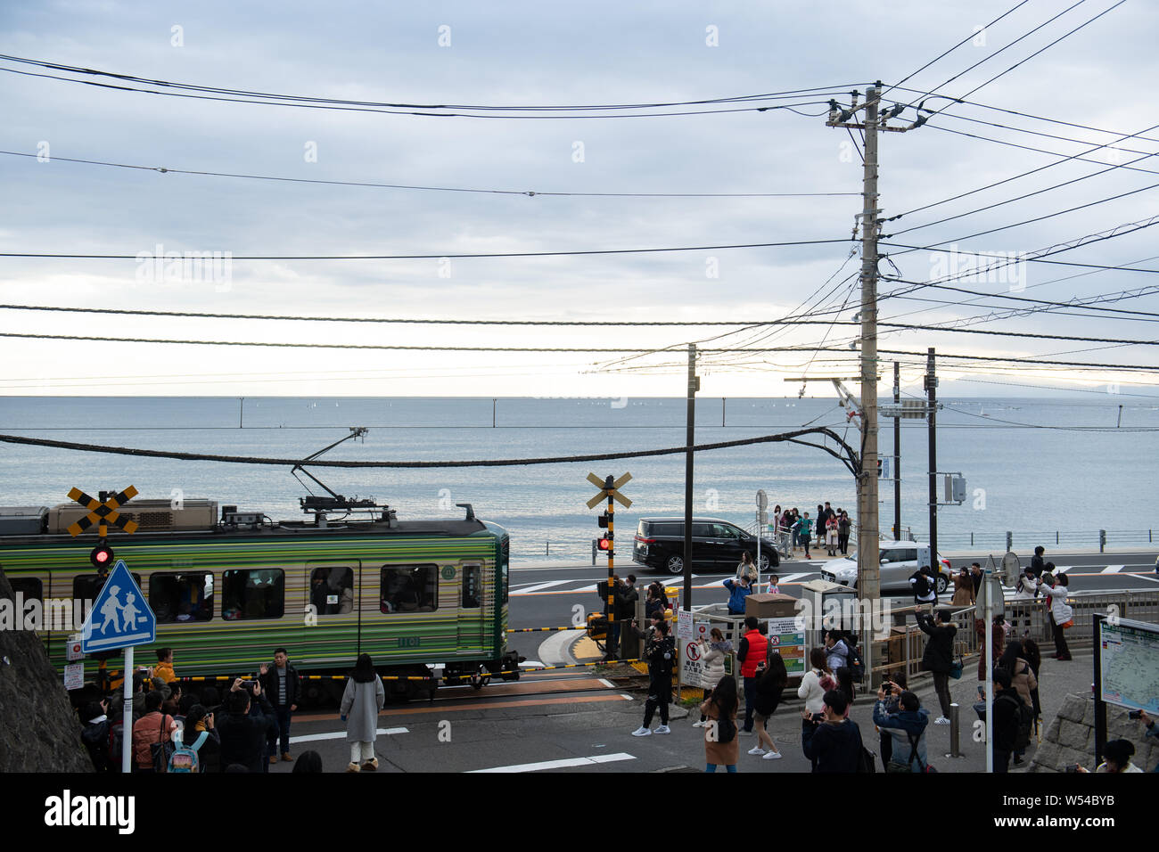 Tourists take photos as a train on the Enoden Line travels past the ...