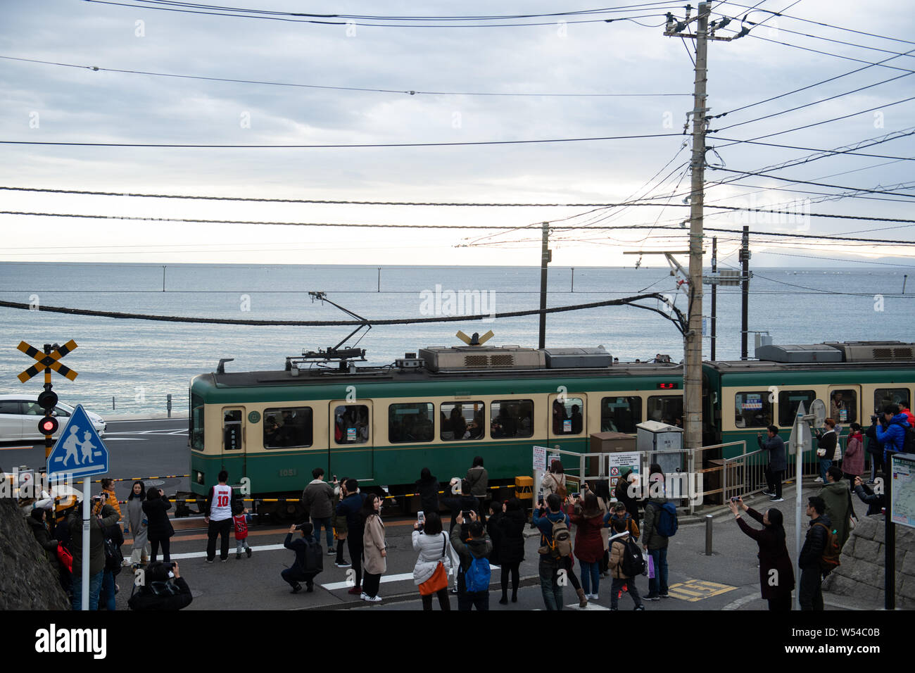 Tourists take photos as a train on the Enoden Line travels past the ...