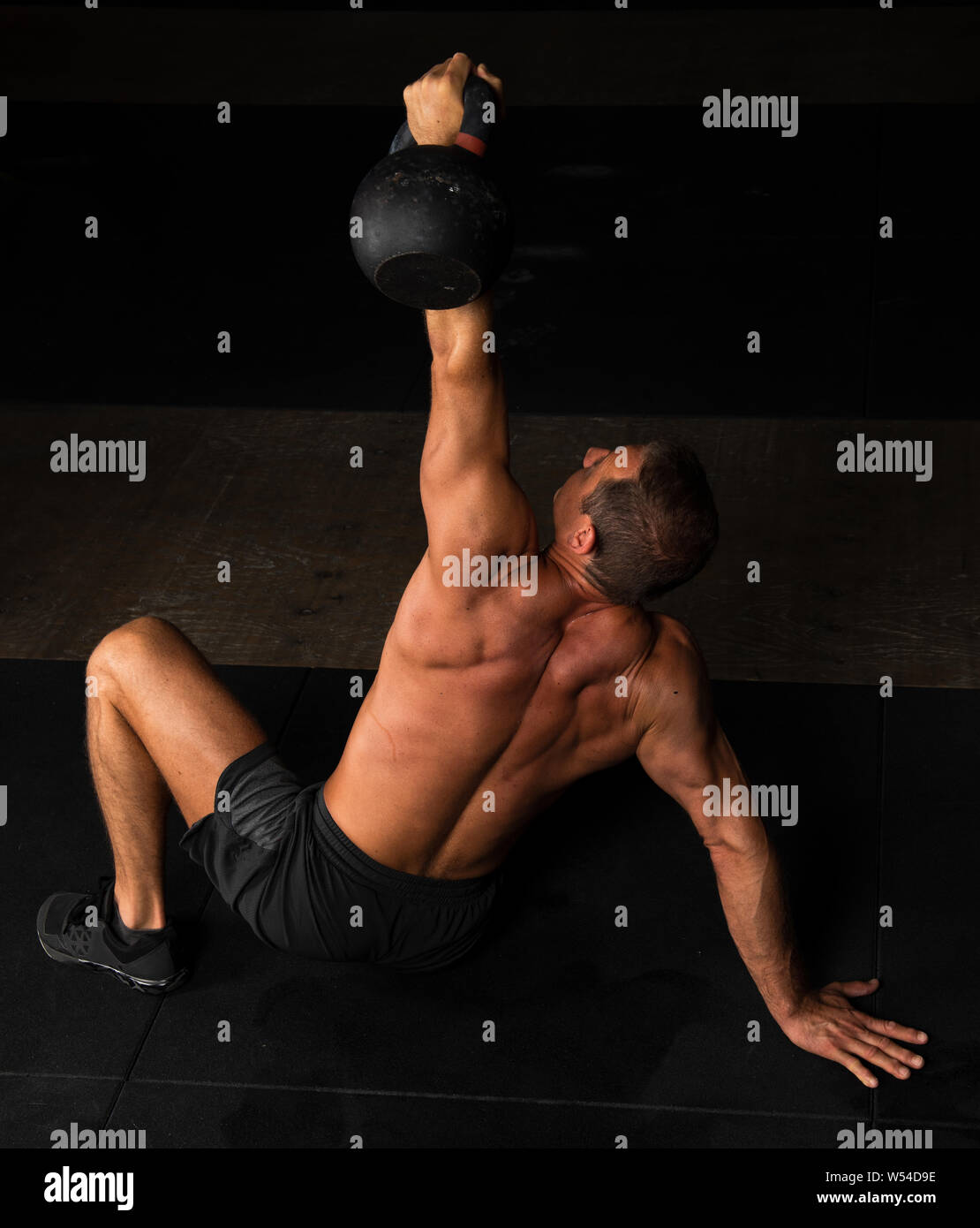 A fit suntanned man with strong back muscles is doing weight lifting ...