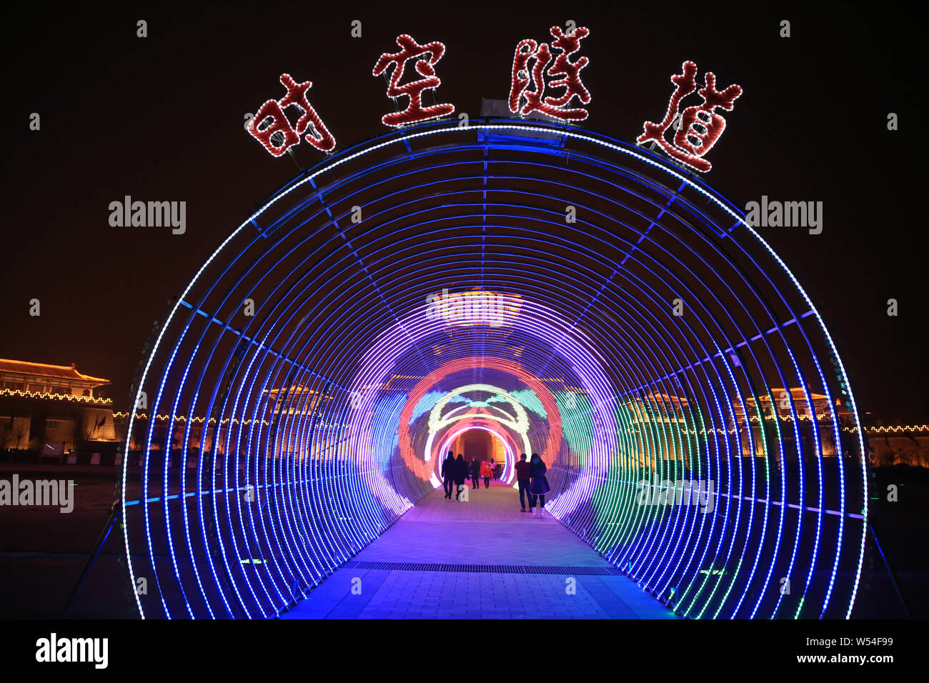 Visitors walk through a tunnel illuminated by colorful lights, which is ...