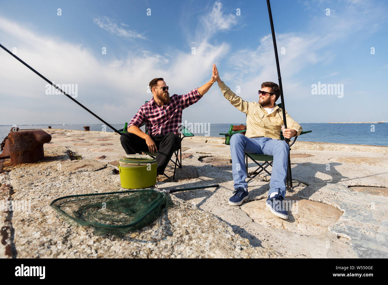 male friends with fishing rods making high five Stock Photo - Alamy