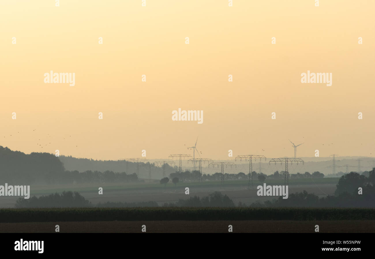 wind turbines and power lines in the distance in hazy hillside in warm ...