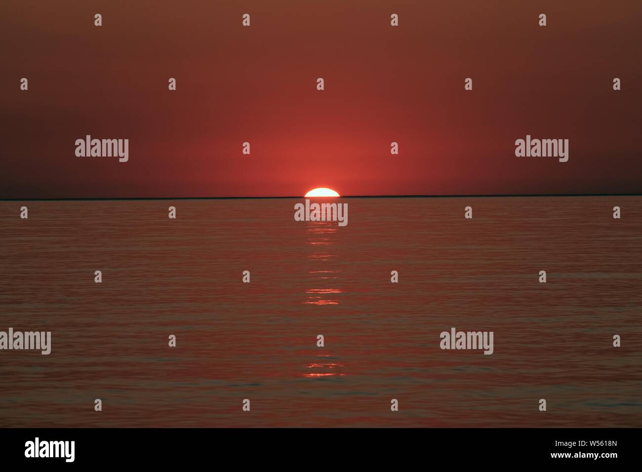Sun behind sea with waves and red sky at sunset Stock Photo - Alamy