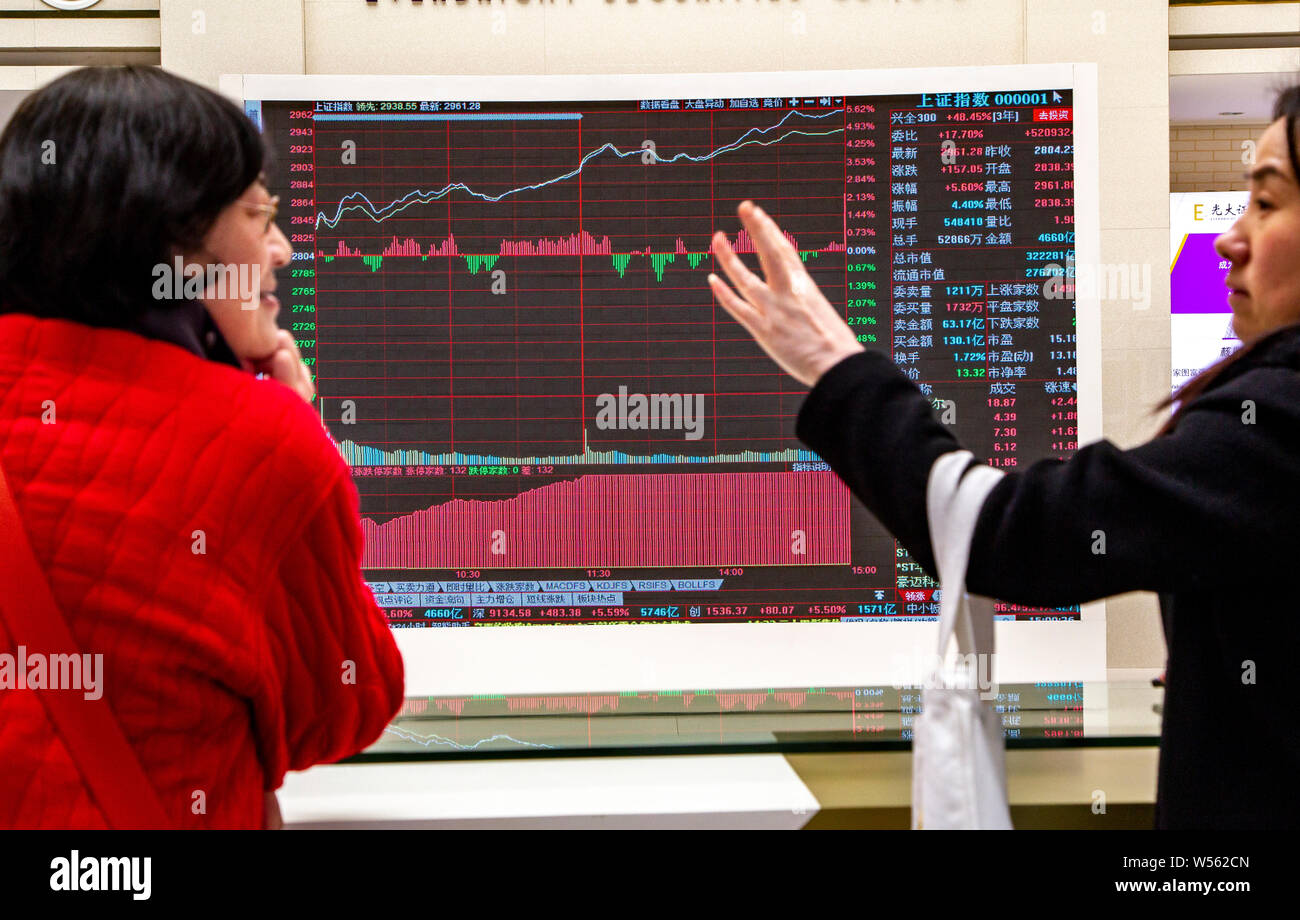 Chinese employees talk in front of a screen displaying stock indices ...