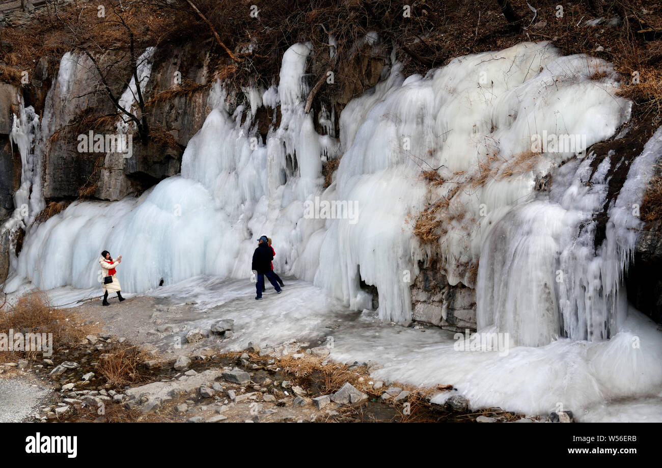 Tourists pose for photos with the icefall scenery at the Shenquan Gorge ...