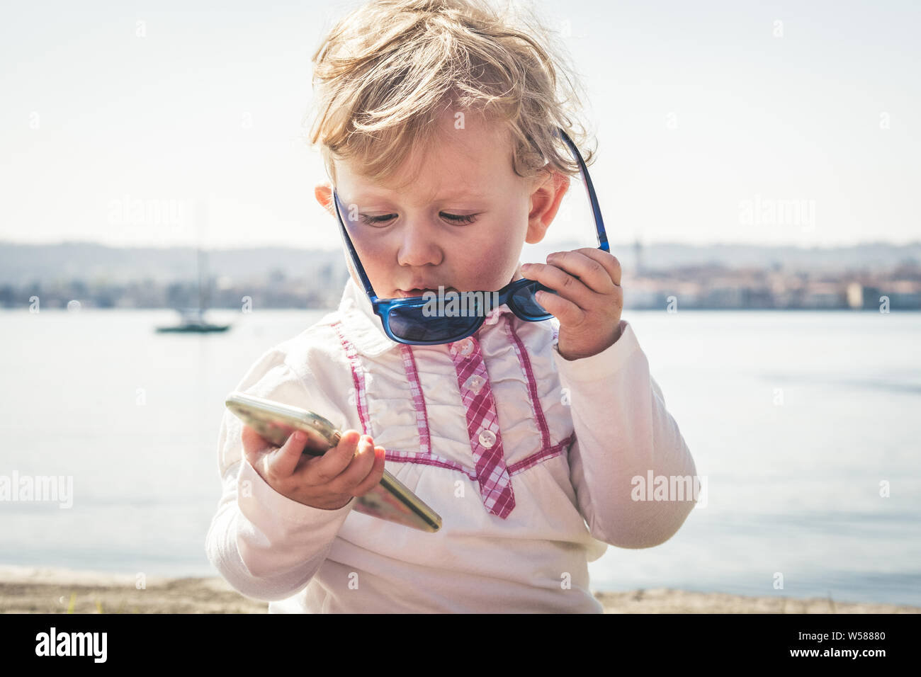 Cute little girl using modern smartphone. Baby holding mobile phone and ...