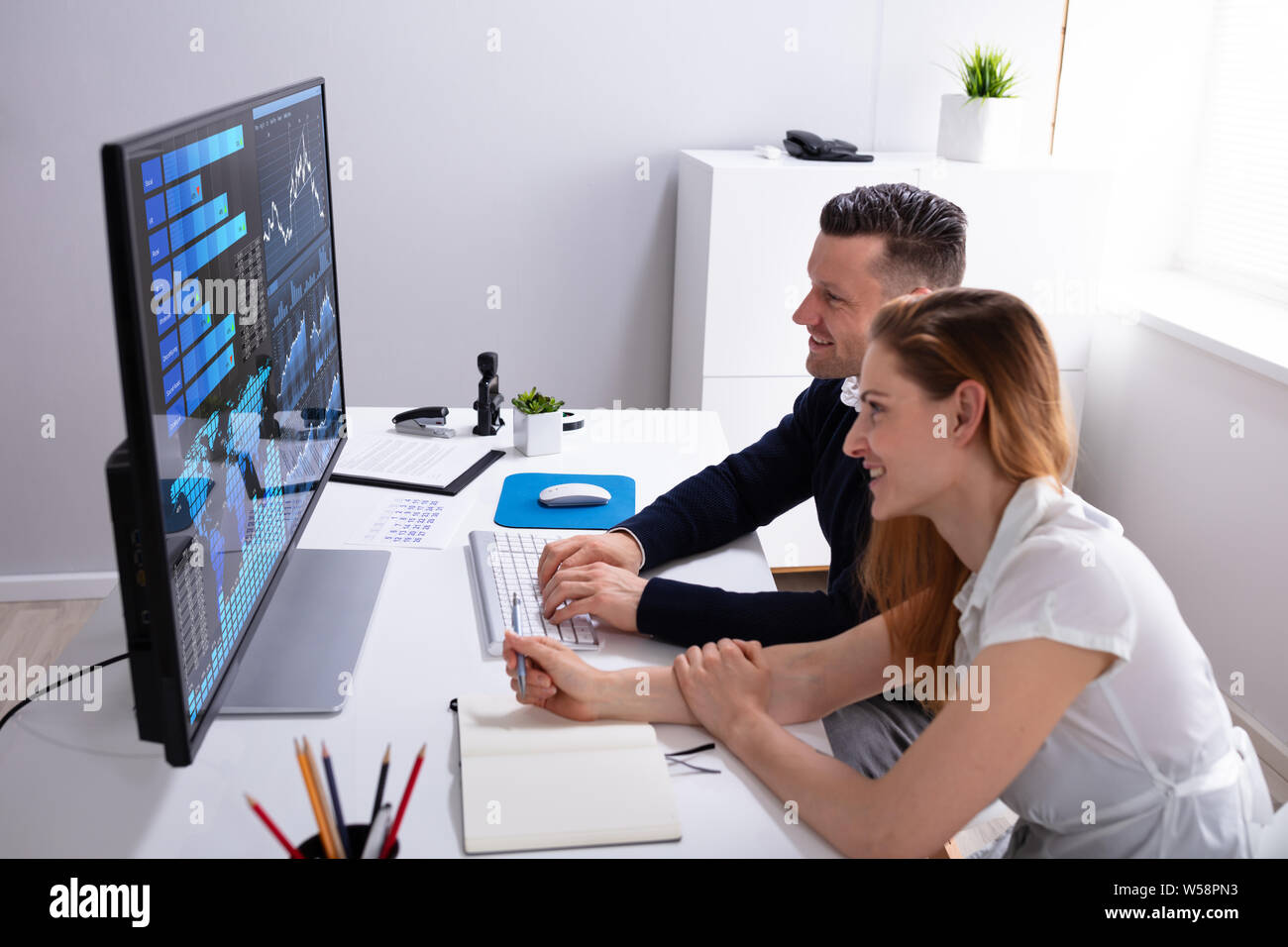 Side View Of Two Smiling Businesspeople Analyzing Bar Graph On Computer ... Side View Of Two Smiling Businesspeople Analyzing Bar Graph On Computer ...