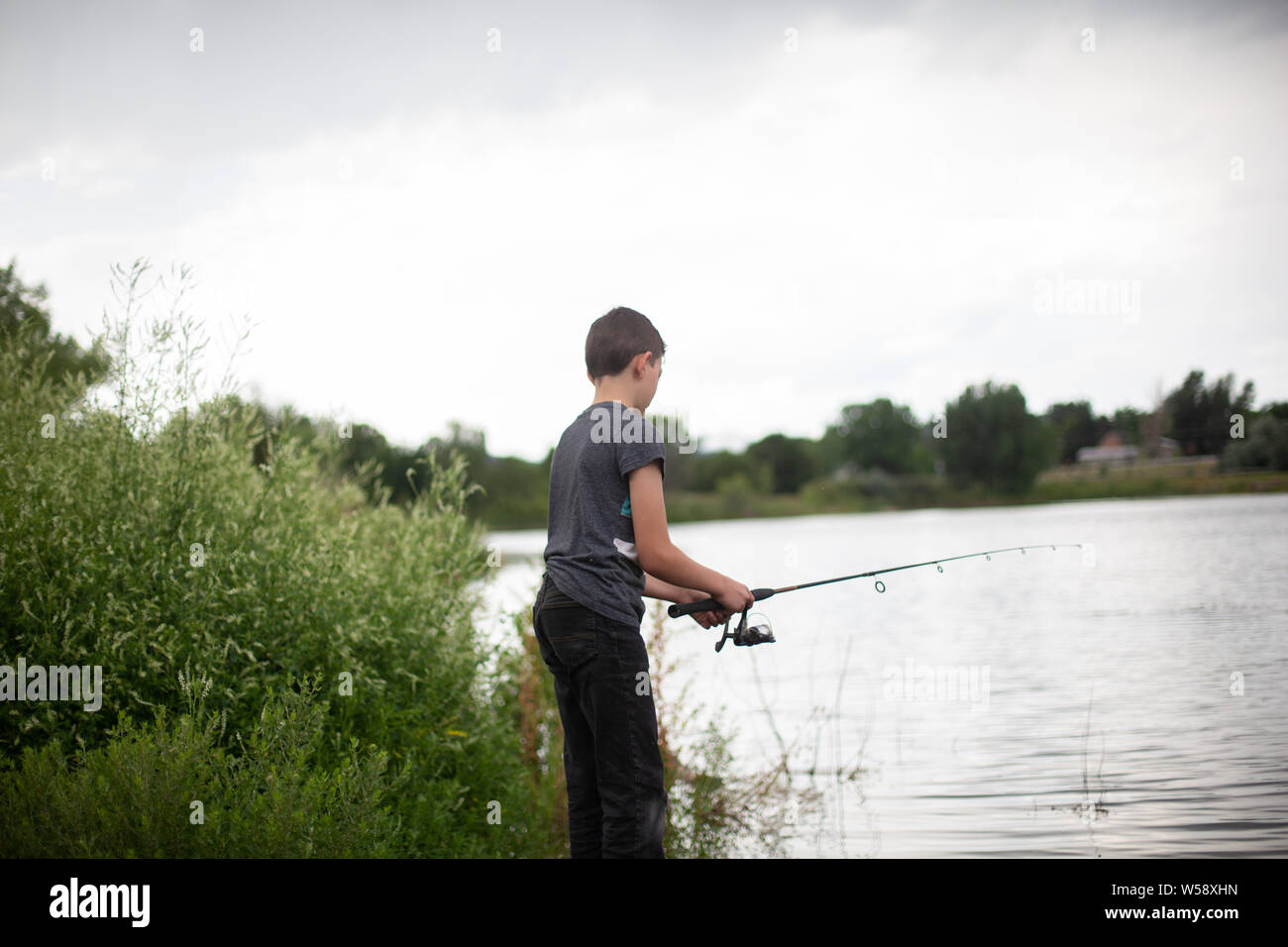 Tween fishing at the edge of a pond surrounded by bushes Stock Photo ...