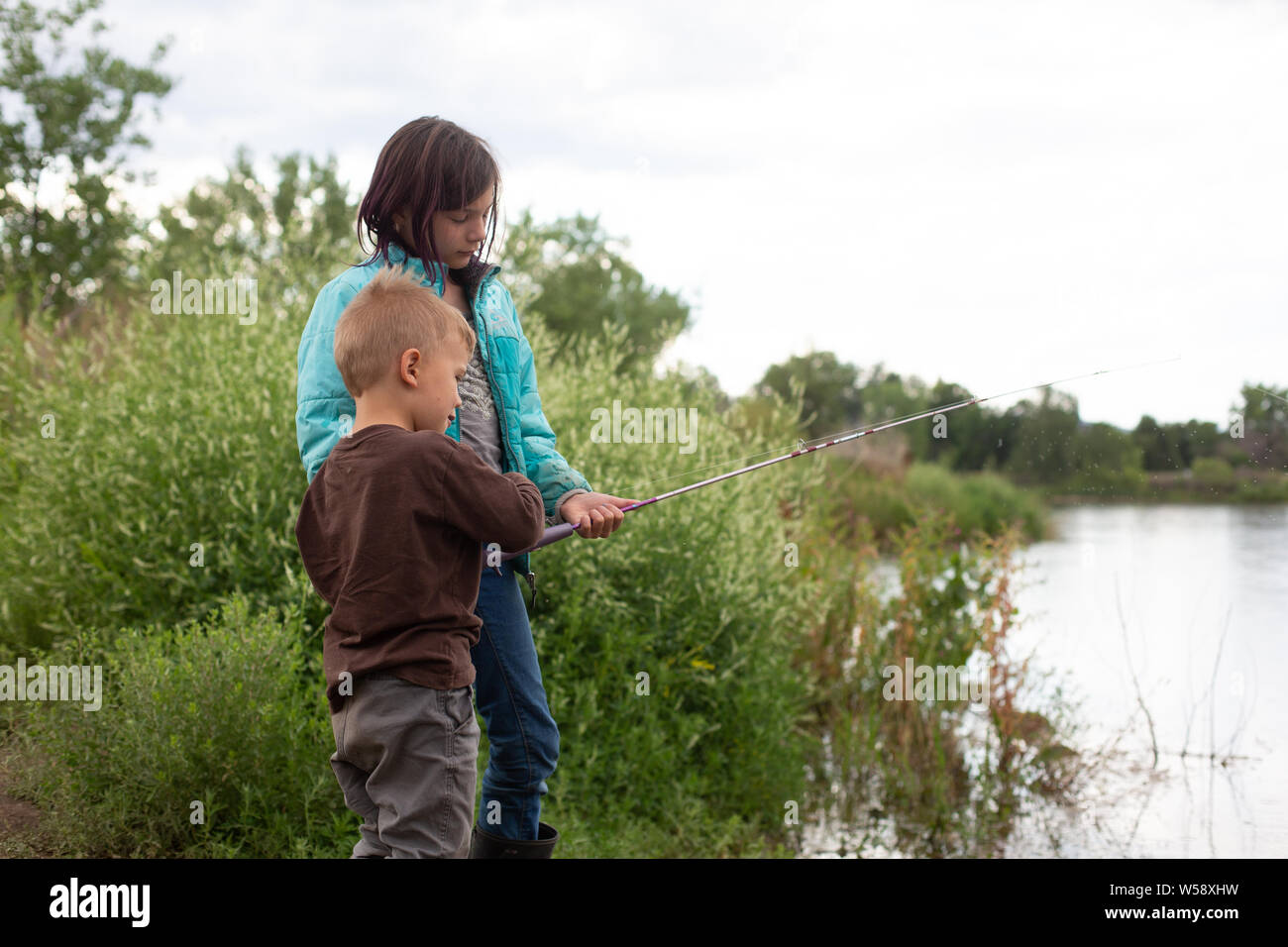 Siblings fishing at a pond, sister helping little brother Stock Photo ...