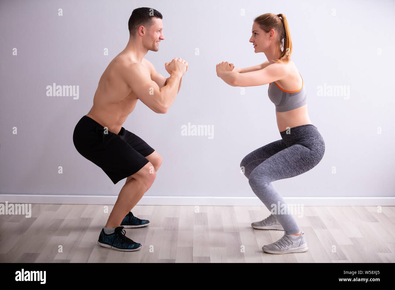 Side View Of Happy Fitness Couple In Sportswear Doing Squat Exercises ...
