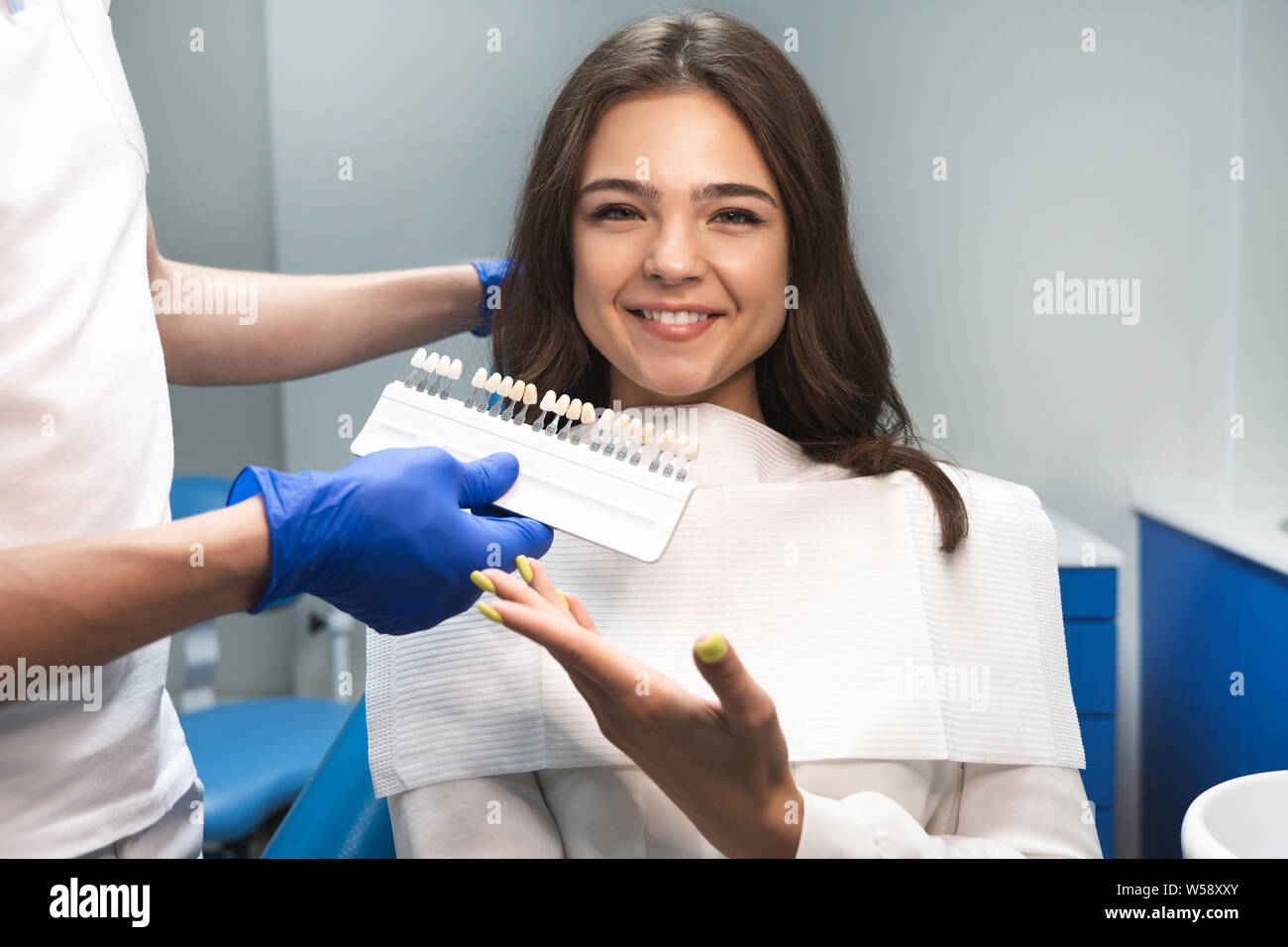 dentist in blue gloves showing tooth enamel scale to smiling woman ...
