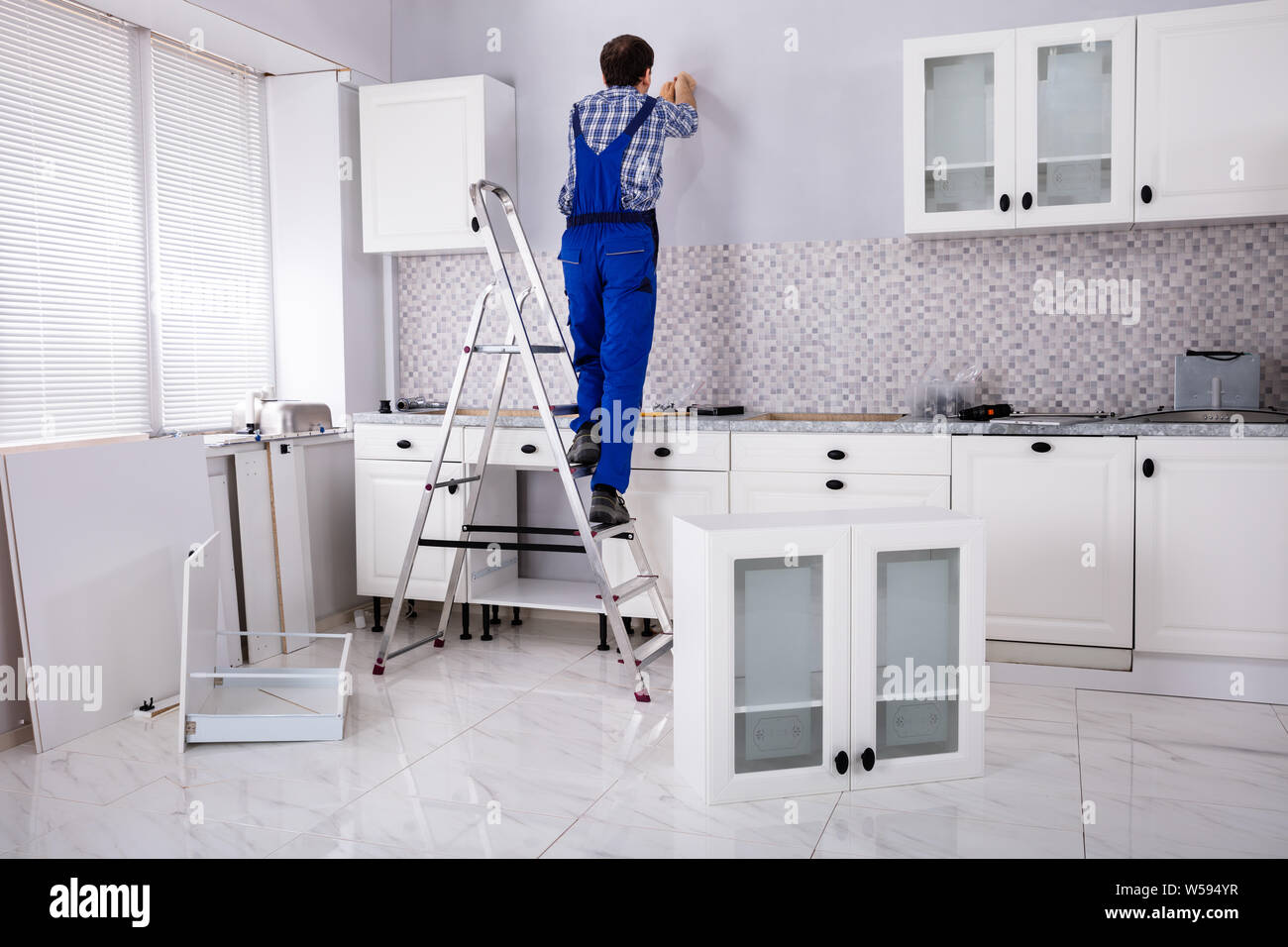 Rear View Of A Male Carpenter Assembling White Cabinet On Wall In ...