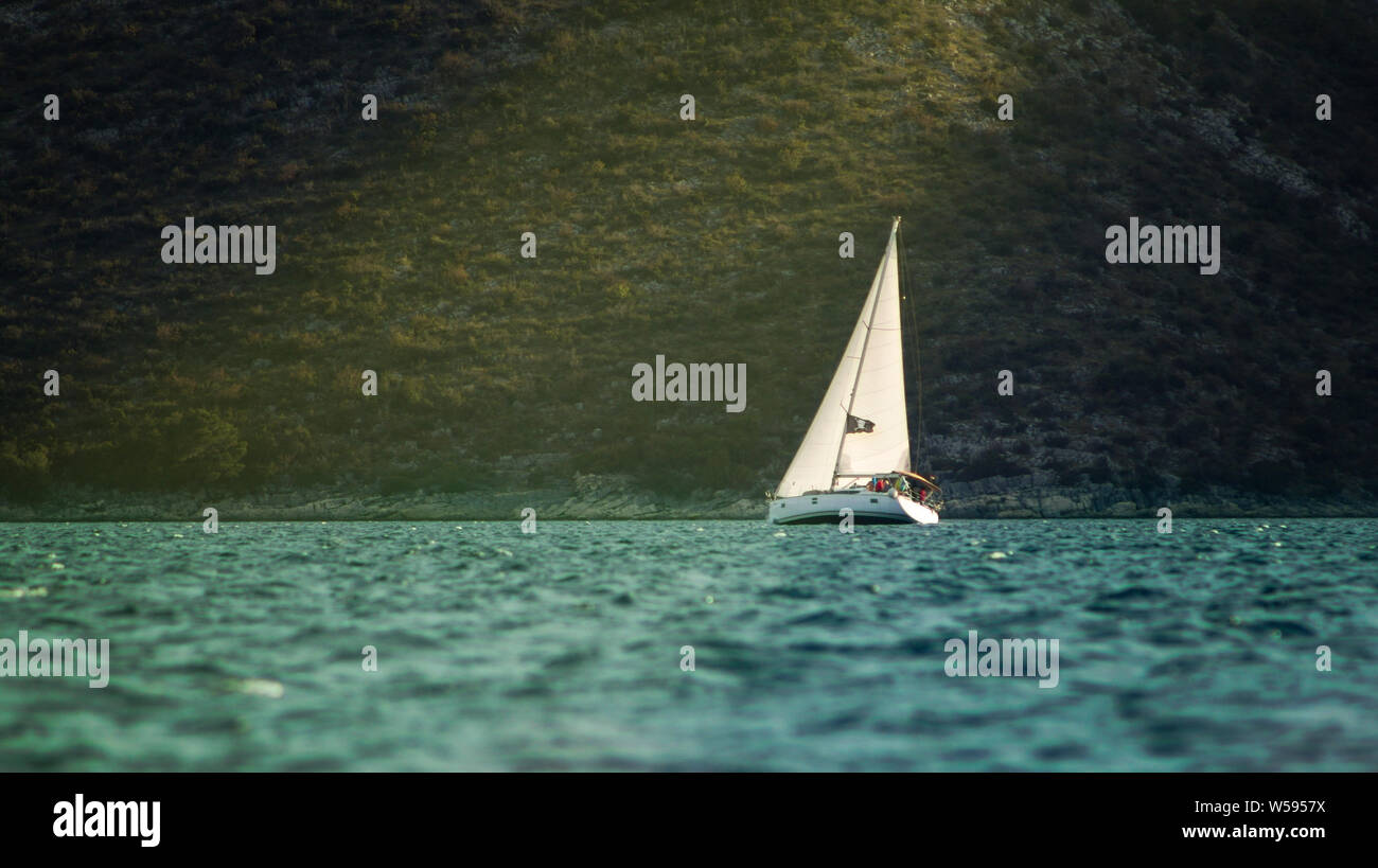 Sailing boat with pirate flag and sunbeam behind it is in reaching ...