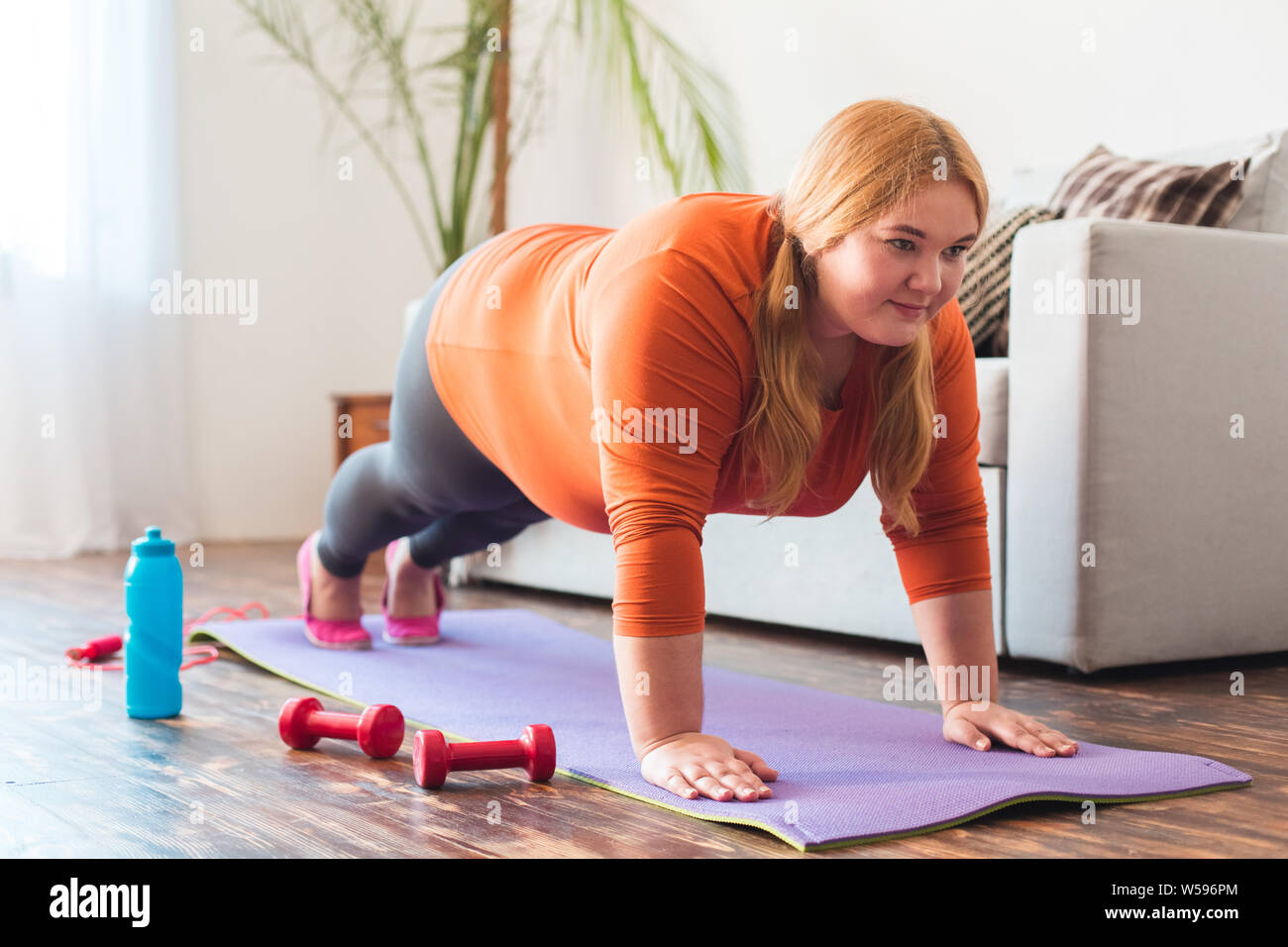 Chubby woman sport at home standing on arms on mat in yoga pose smiling ...