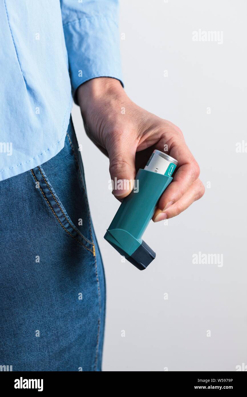 Close-up of hand holding an asthma inhaler. The inhaler contains ...